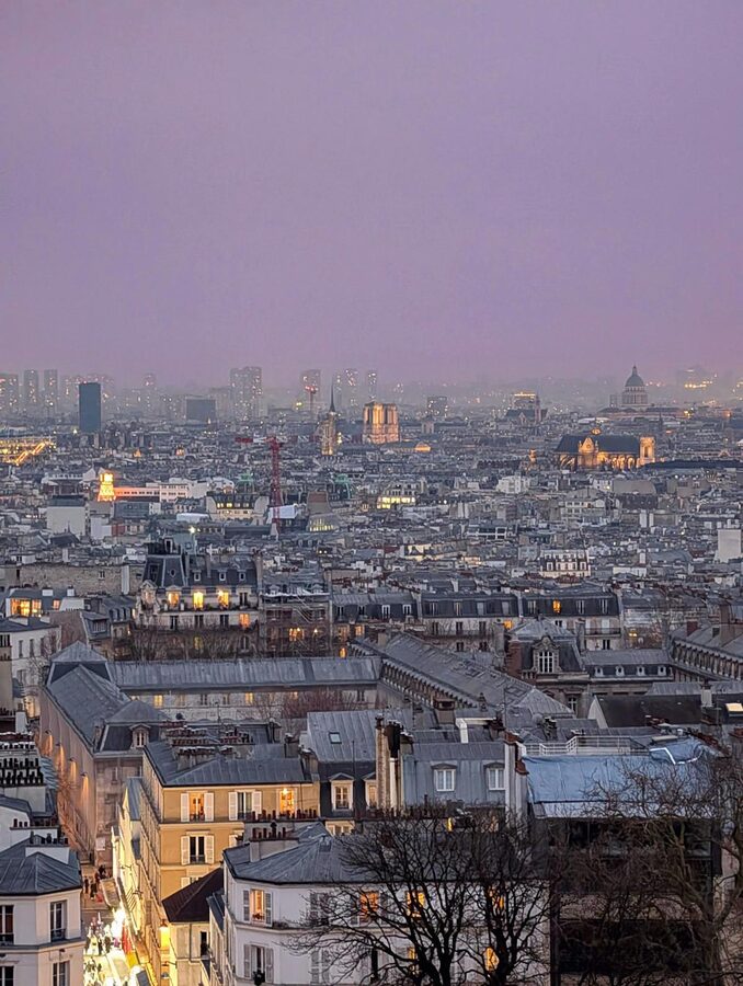 Paris rooftops at twilight with warm glowing lights across the city