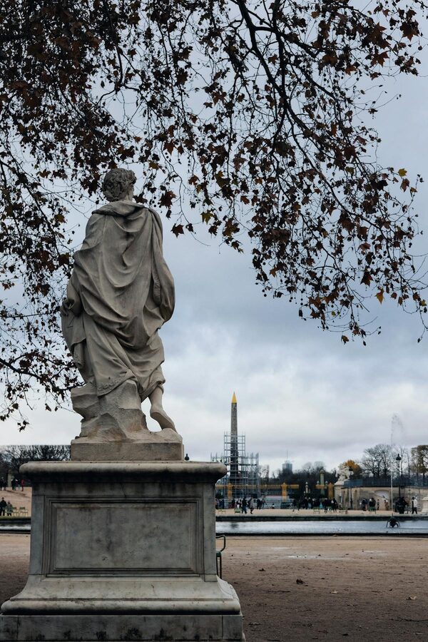 Marble statue in the Tuileries Garden with the Luxor Obelisk visible in the background