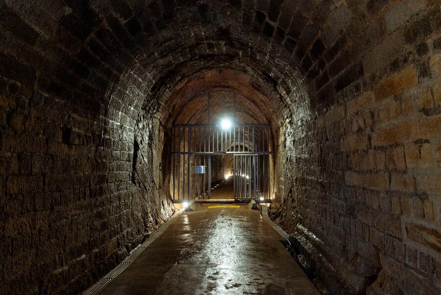 An illuminated stone tunnel with a metal gate