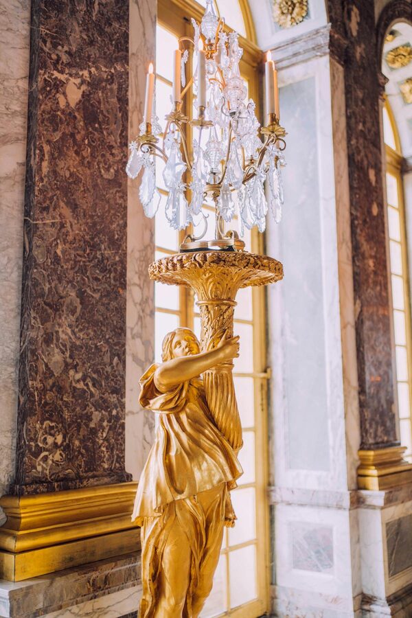 A golden sculpture holding a chandelier inside the Palace of Versailles