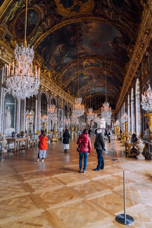 The Hall of Mirrors at Versailles with visitors walking through the ornate gallery