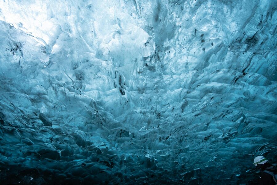 Visitors walking through a crystal blue ice cave interior