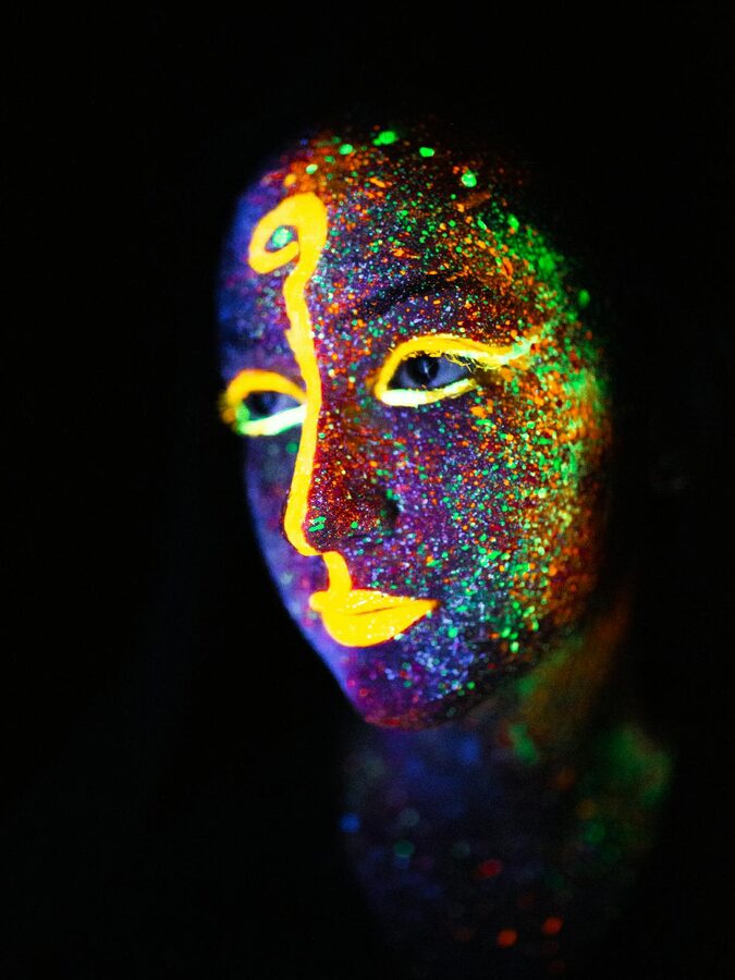 Face painted with neon colors under black light close-up