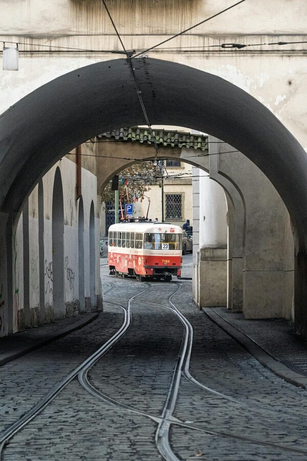 Red tram passing through historic arched tunnel in Prague