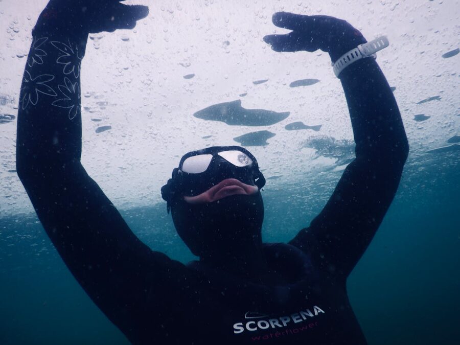 Diver swimming under ice in cold water