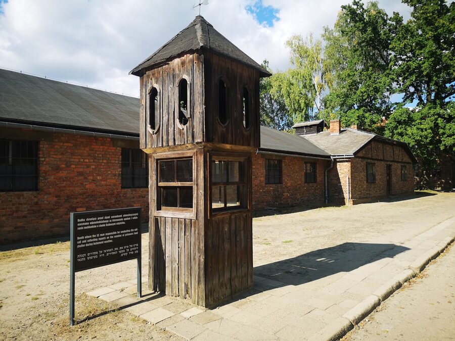 Wooden guard tower in front of brick buildings at a concentration camp memorial site