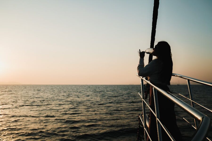 Person enjoying a drink on the deck of a sailboat at sunset
