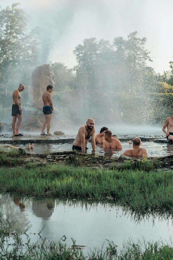 Group relaxing in natural hot springs surrounded by greenery