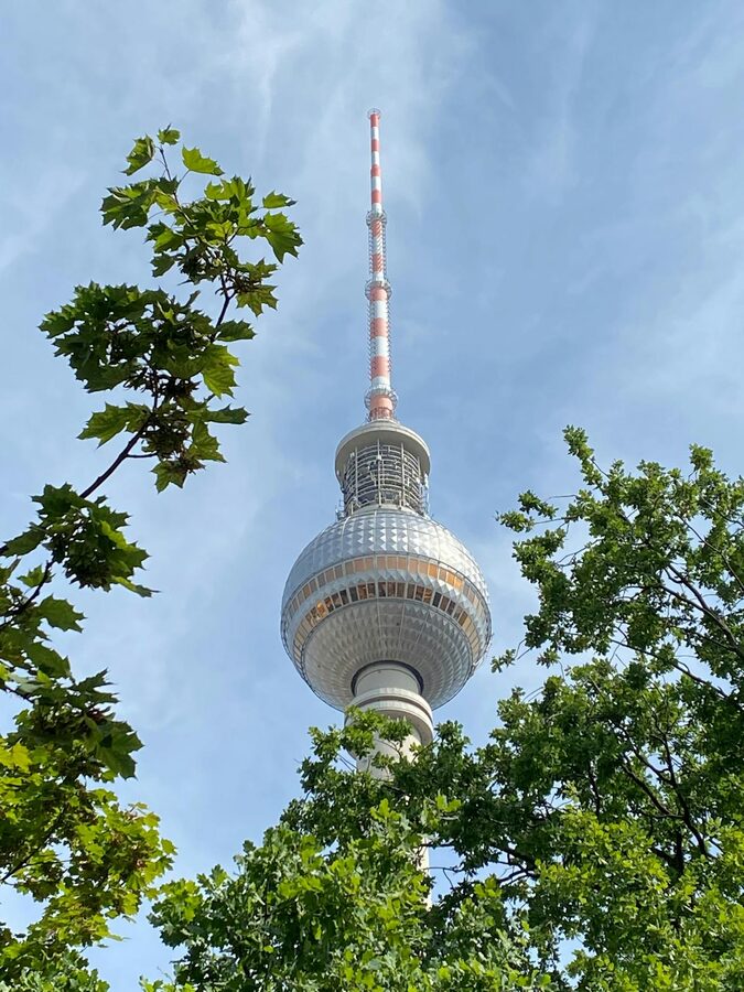 Berlin TV Tower seen through green tree leaves against blue sky