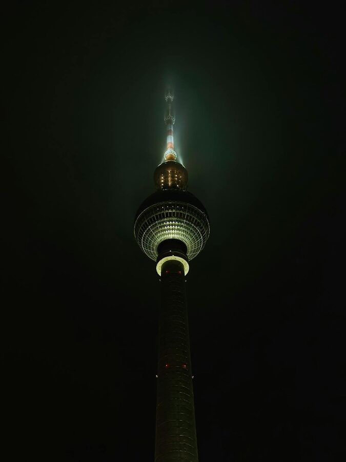 Berlin TV Tower illuminated against dark night sky with dramatic lighting