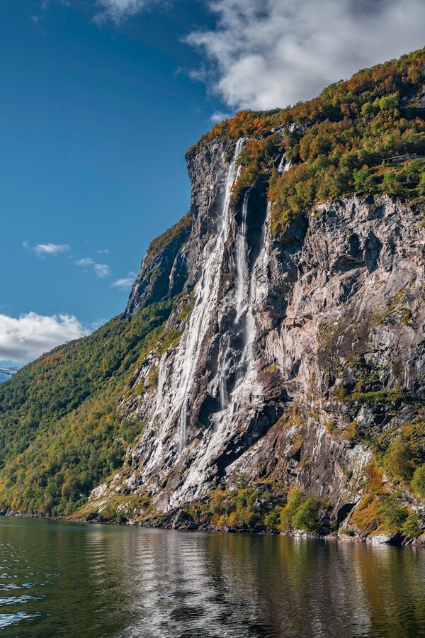 Waterfall streaming down steep cliff into a Norwegian fjord