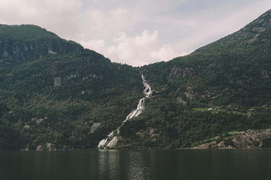 Waterfall flowing through green mountains into a peaceful Norwegian lake